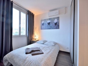 Quarto de hotel com cama, mesa de cabeceira, ar condicionado fixado na parede e janela com cortinas.