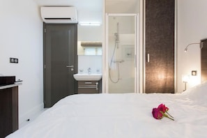 Quarto de hotel com cama, chuveiro, pia e porta escura.