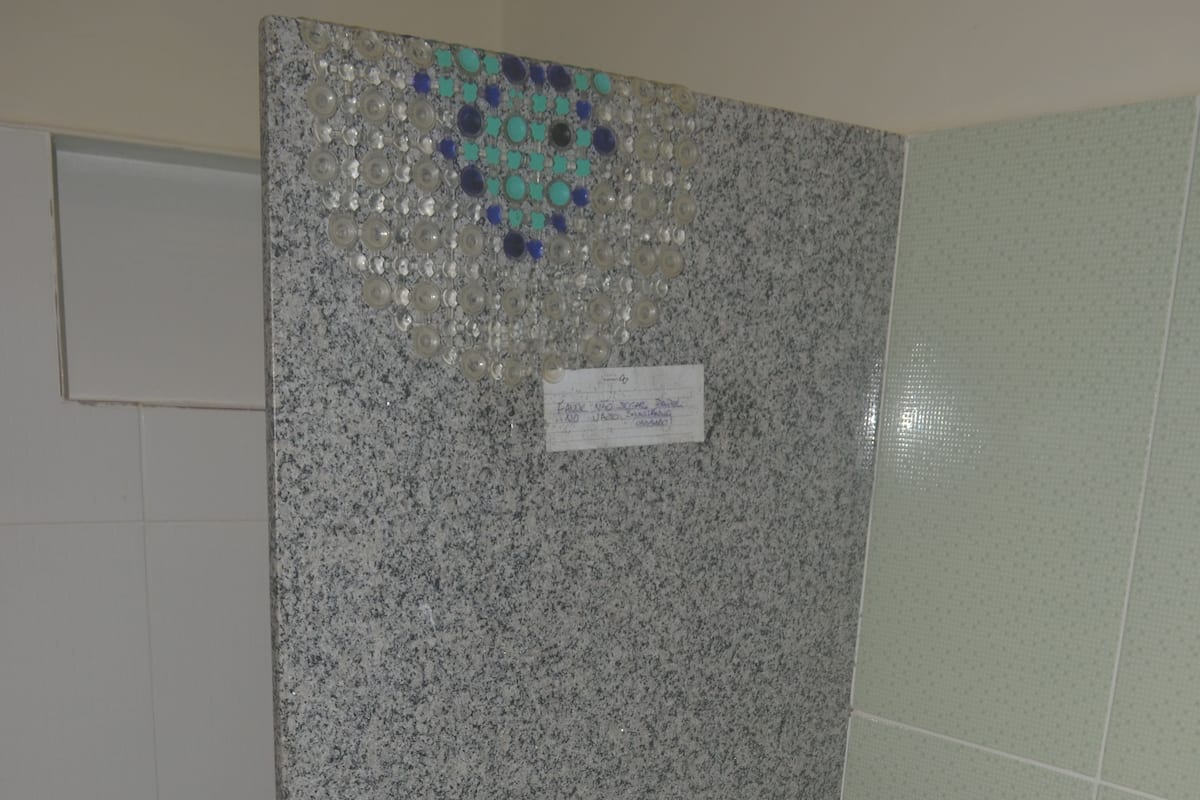 Casa de banho com sanita branca, cabine de duche com mosaico decorativo e parede revestida a azulejos.