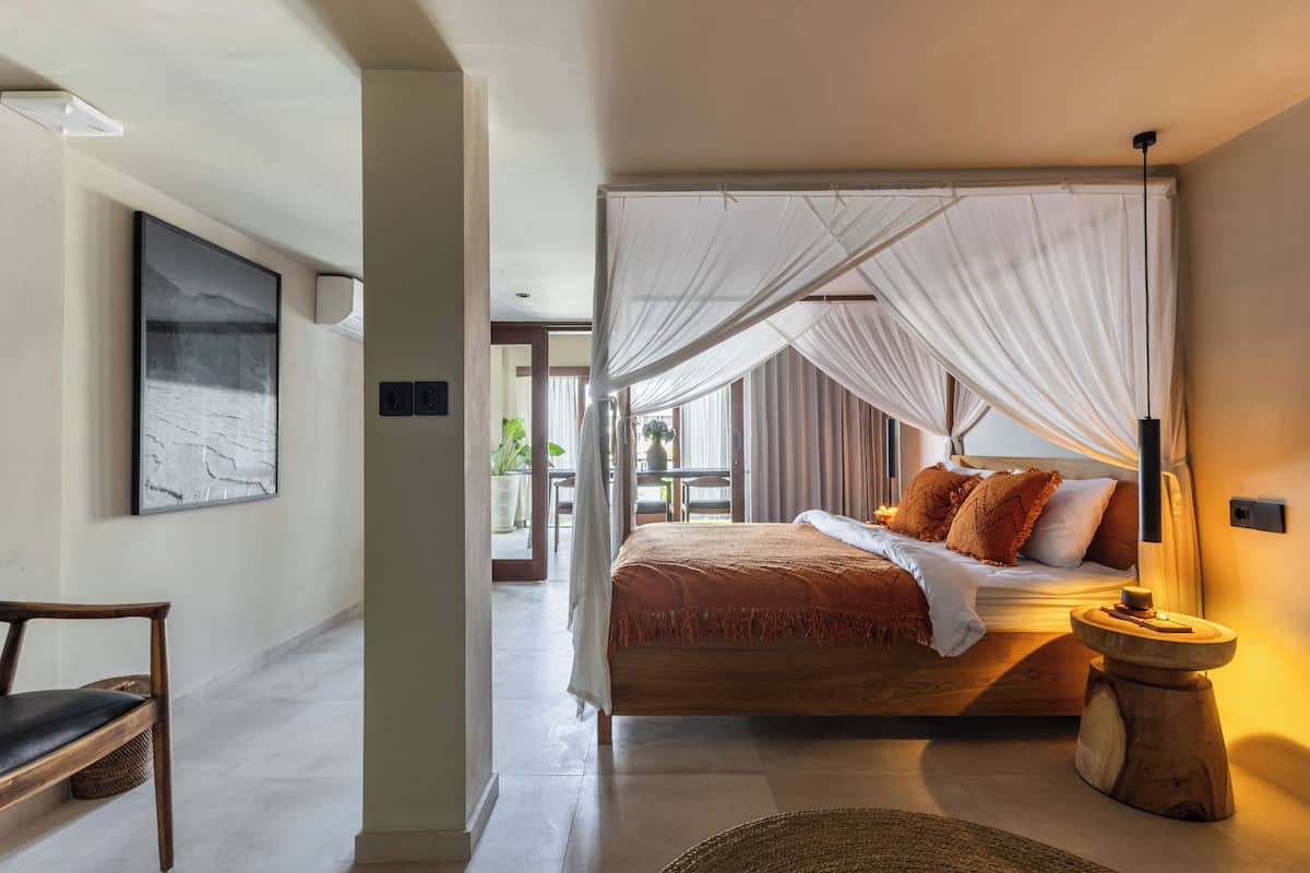 Quarto com cama de dossel, um banco de madeira, mesa de cabeceira e um quadro grande emoldurado na parede.