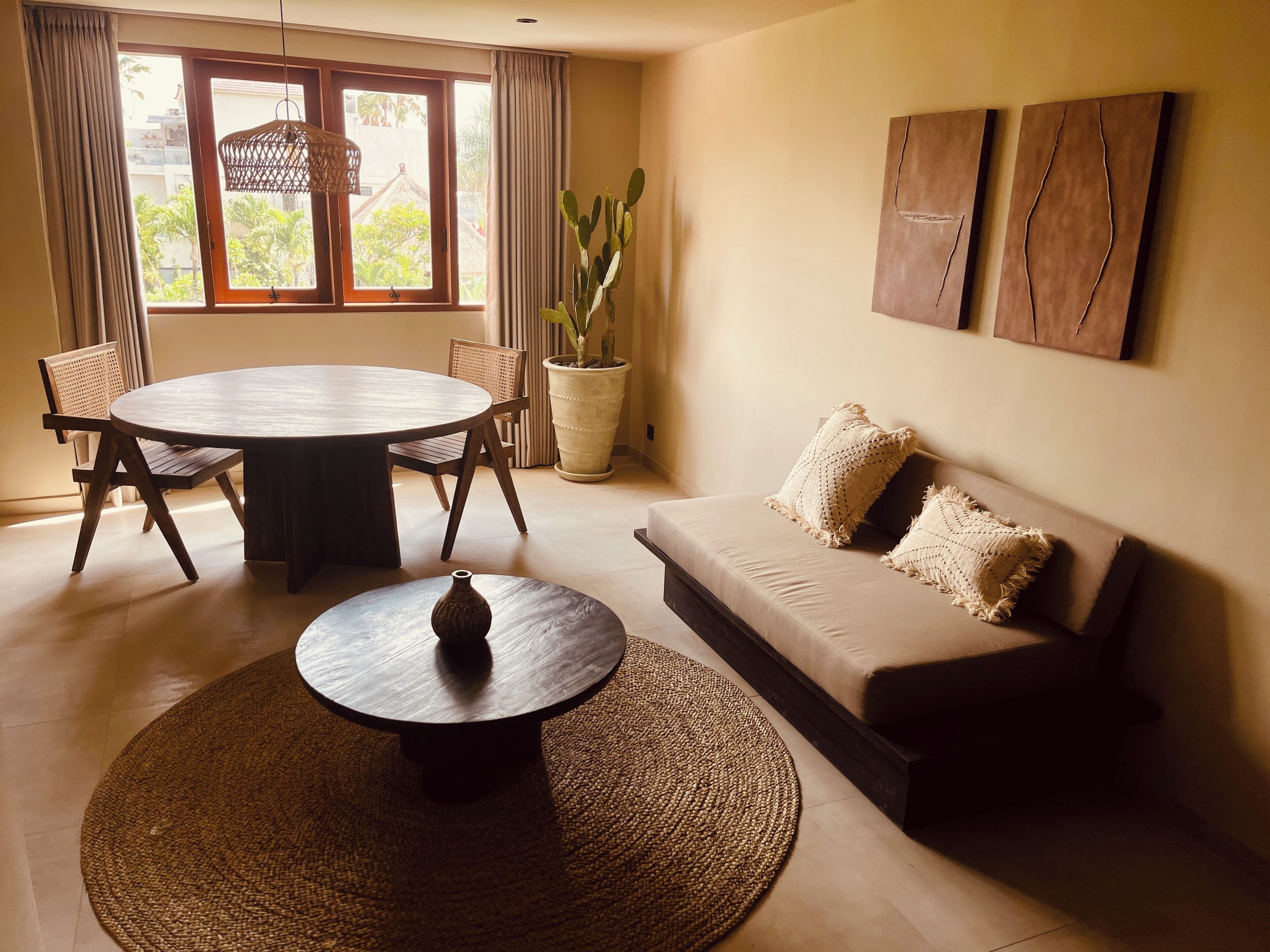 Uma sala de estar com uma mesa redonda de madeira, um sofá e uma grande planta em vaso.