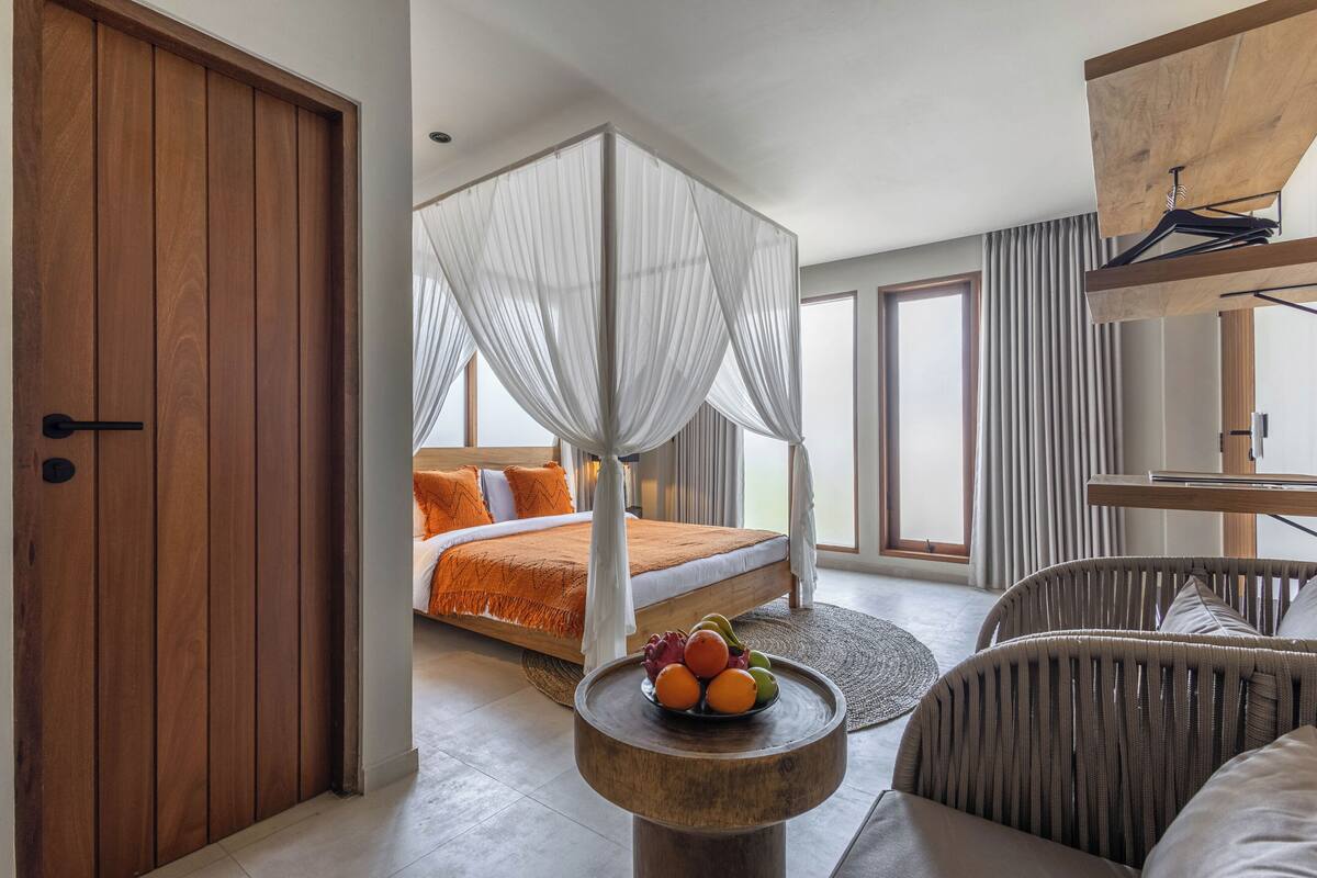 Quarto com cama, mesa de cabeceira com frutas, cadeira suspensa e guarda-roupa.