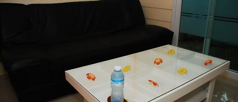 Um quarto com uma mesa de centro de vidro, um sofá preto e uma garrafa de água.