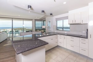 Uma cozinha moderna com uma ilha grande, armários brancos e vista para o oceano.