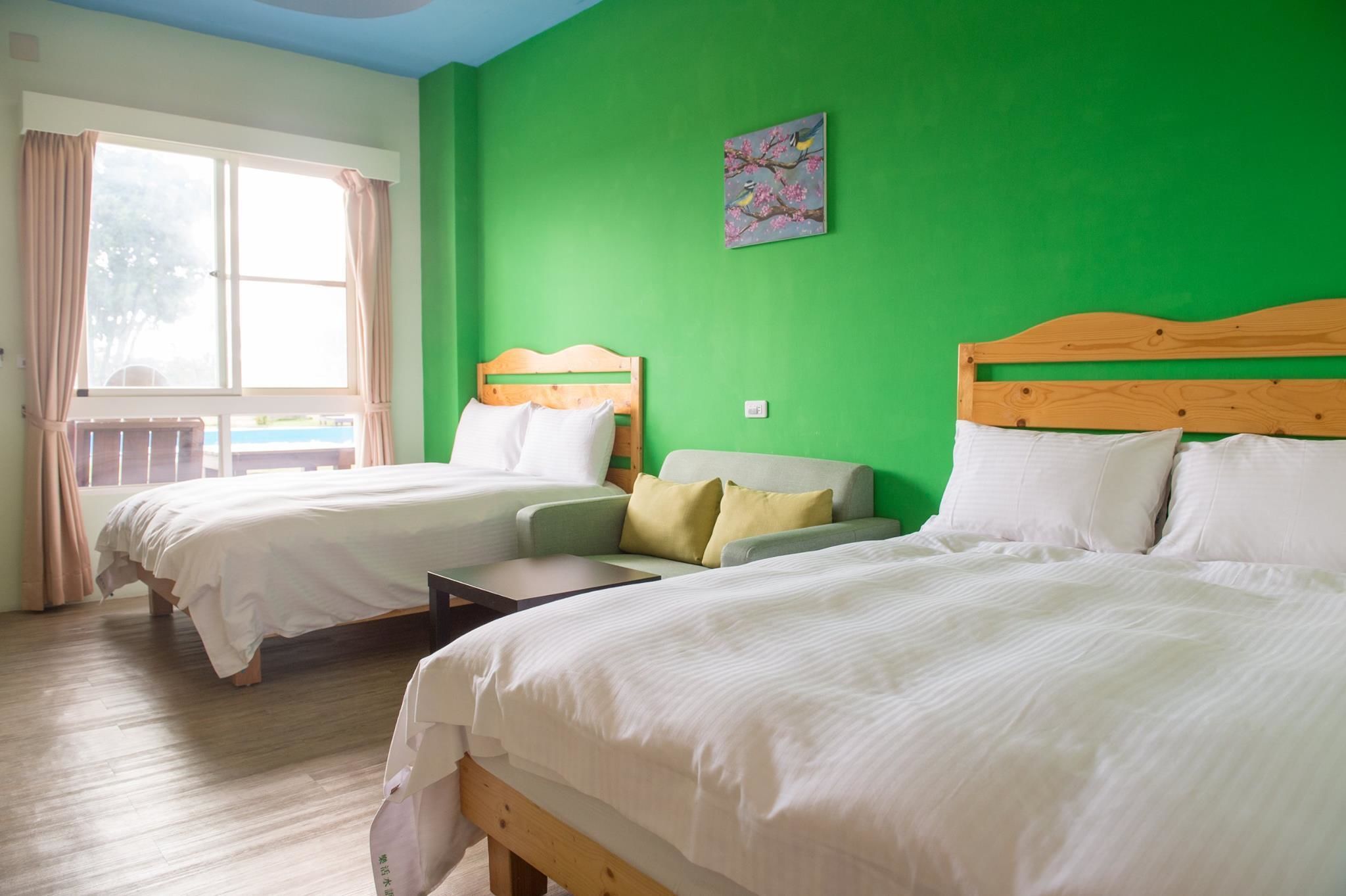 Um quarto com duas camas, uma parede verde, uma janela com cortinas e um quadro.