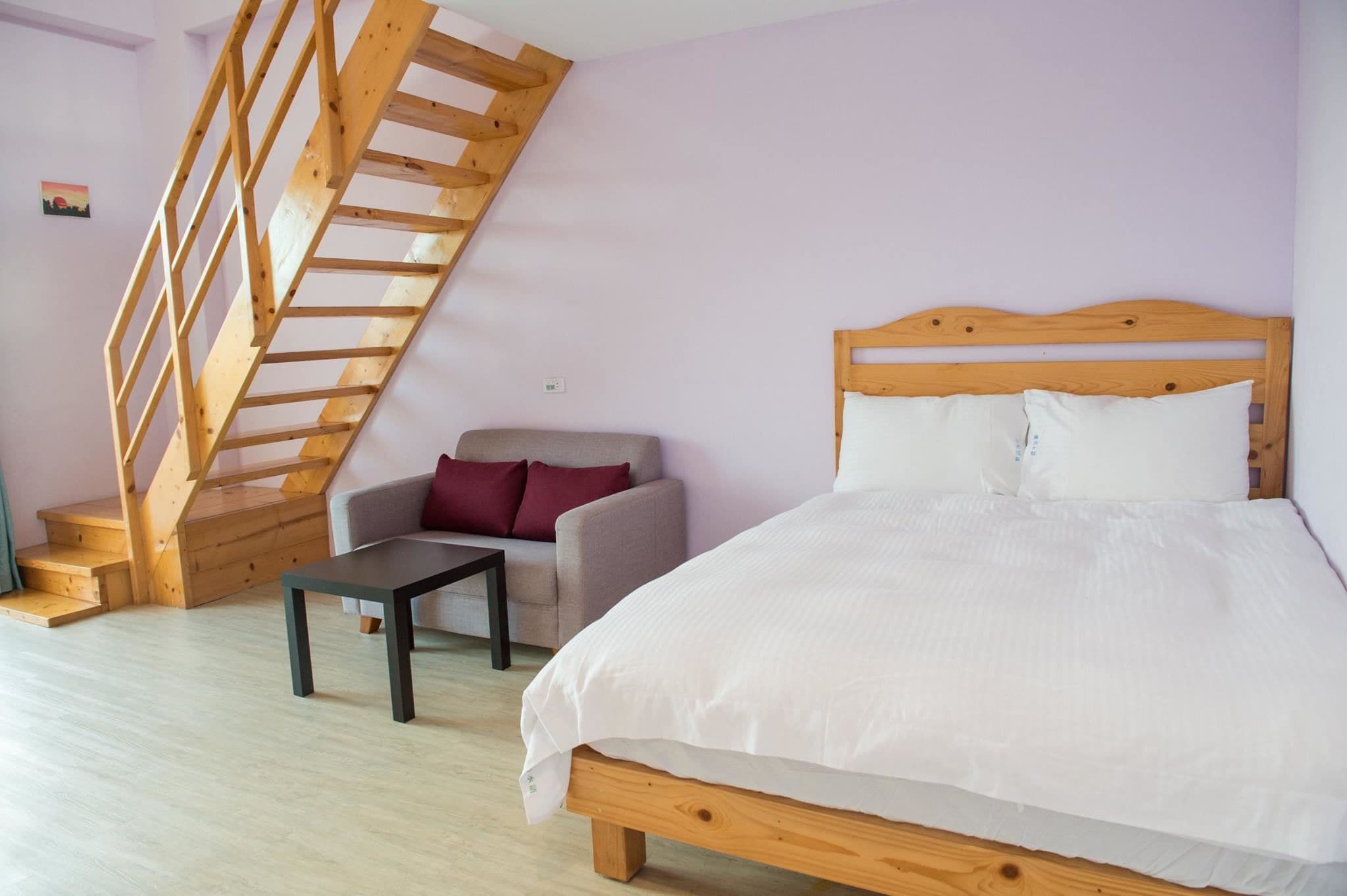 Quarto com cama de madeira, sofá cinzento, mesa pequena e escada de madeira.