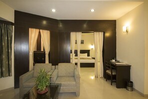 Quarto de hotel moderno com sofá, uma mesinha com planta, escrivaninha com cadeira e cama com cortinas.
