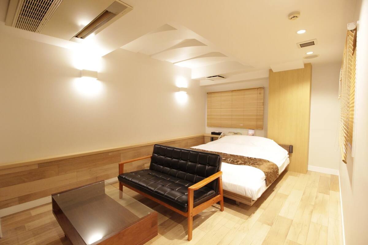 Quarto de hotel com cama, sofá, mesinha e piso de madeira.