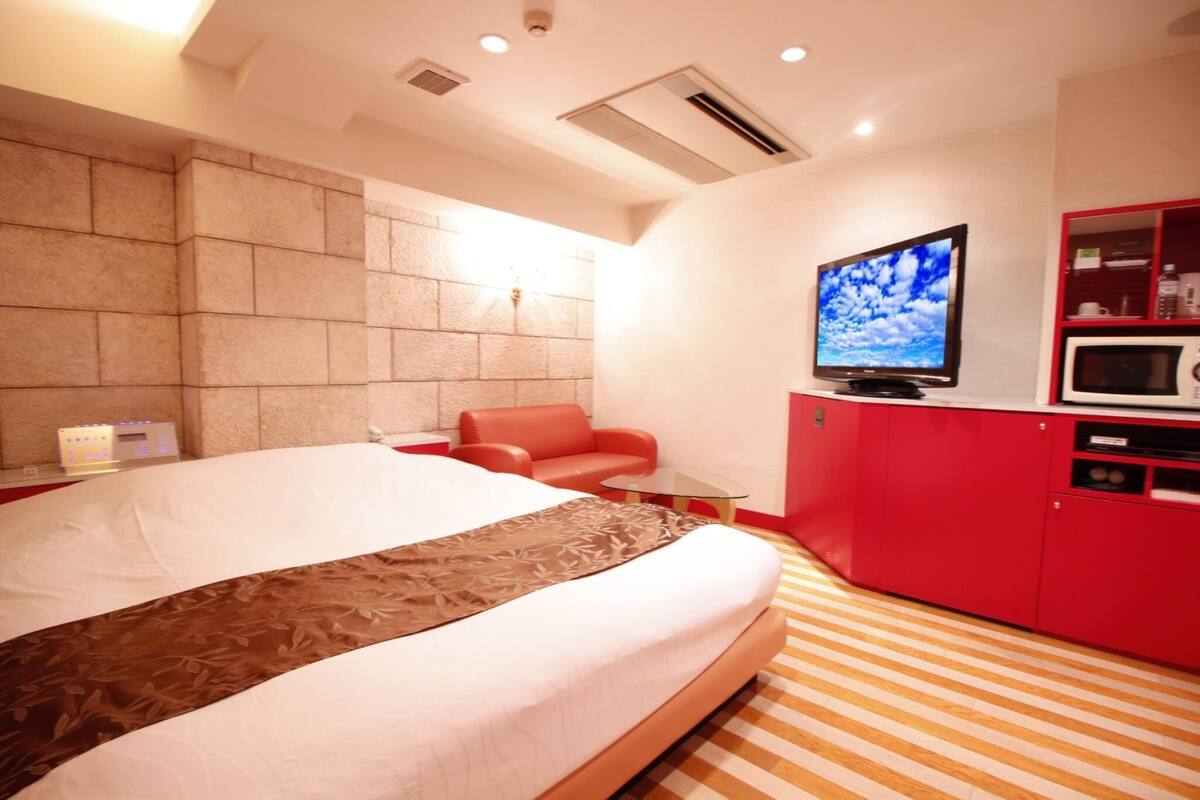 Quarto de hotel com uma cama grande, televisão, micro-ondas e um armário vermelho.