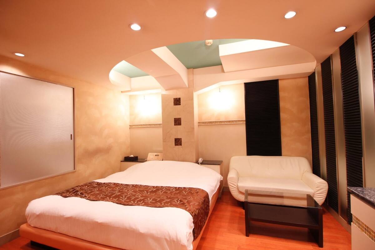 Quarto de hotel com cama, uma cadeira, escrivaninha e uma janela grande.
