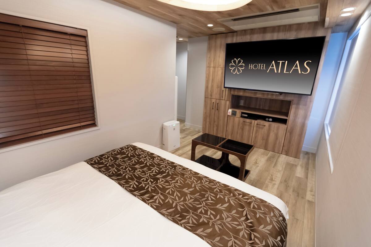 Quarto de hotel com uma cama, uma televisão na parede e uma pequena mesa.