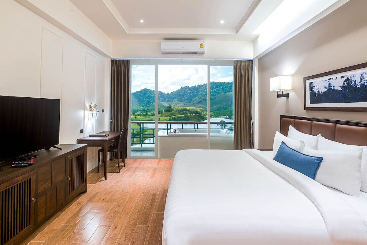 Quarto de hotel com cama grande, televisão, escrivaninha e varanda com vista panorâmica.