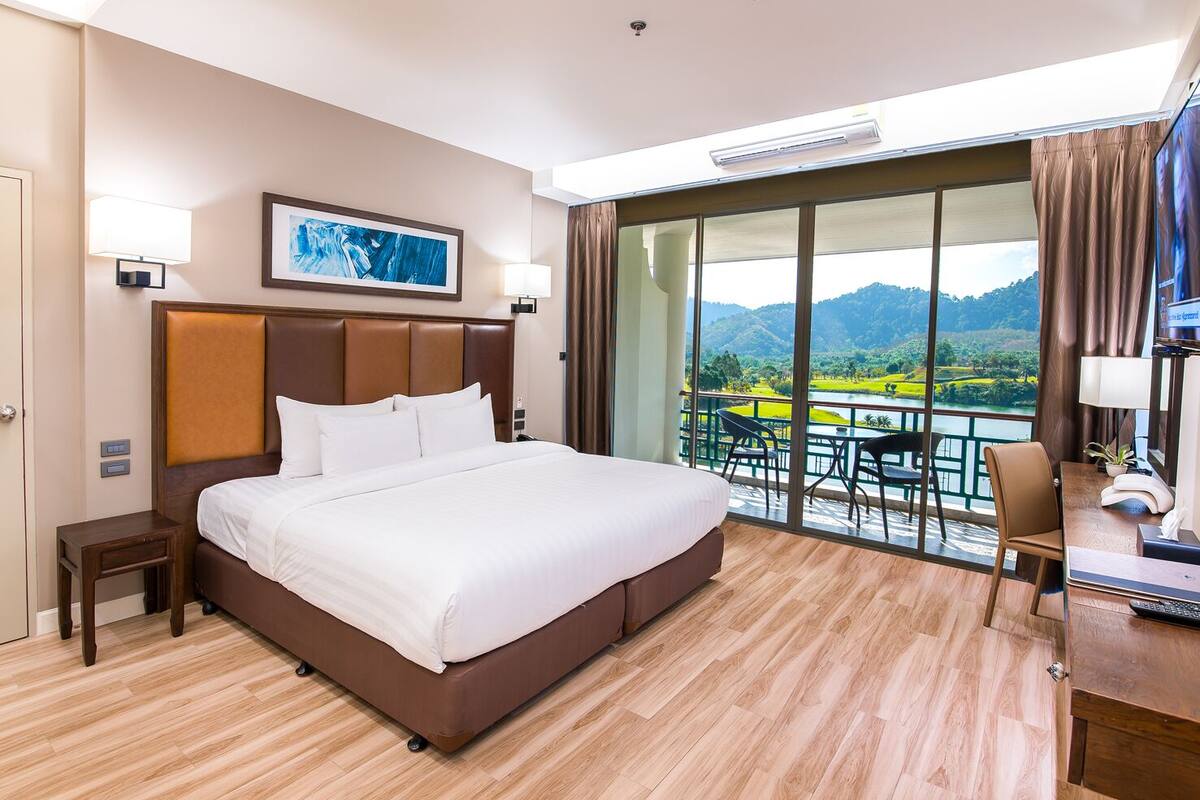 Quarto de hotel com uma cama grande, uma escrivaninha com cadeira, vista para um campo de golfe e um quadro na parede.
