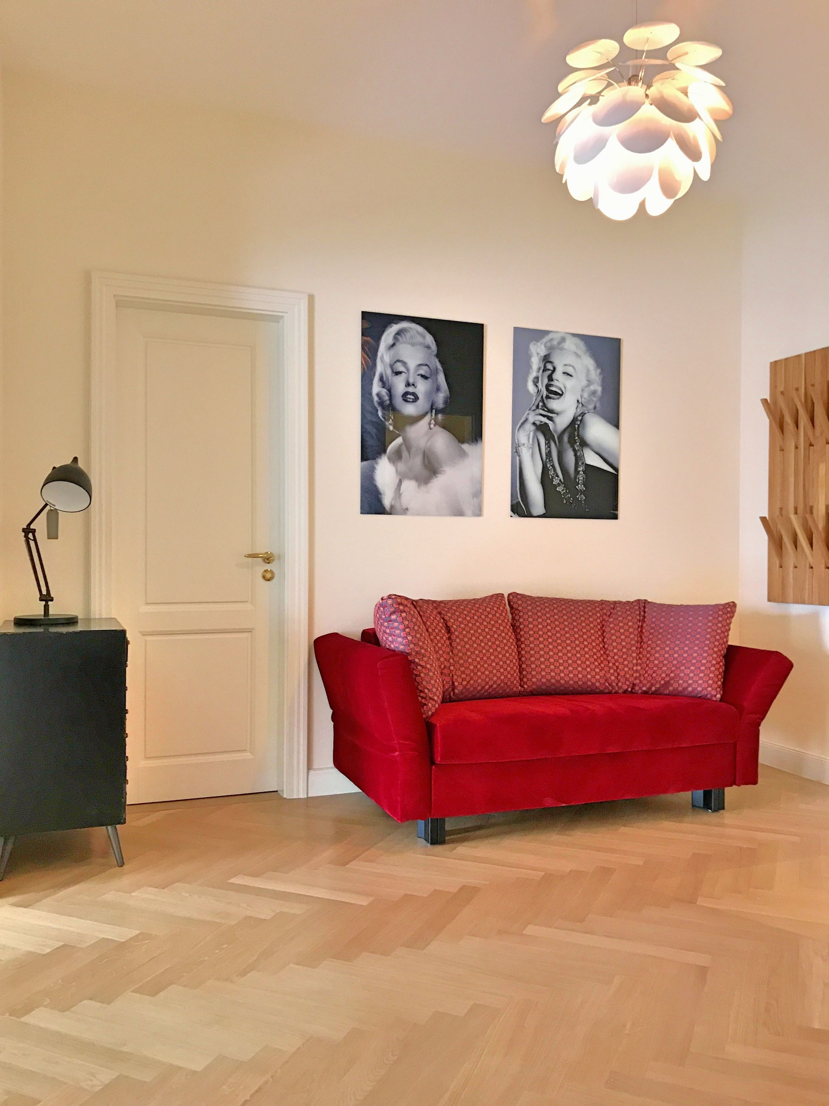 Um quarto com um sofá vermelho, uma mesa lateral preta, uma luminária e duas quadros na parede.