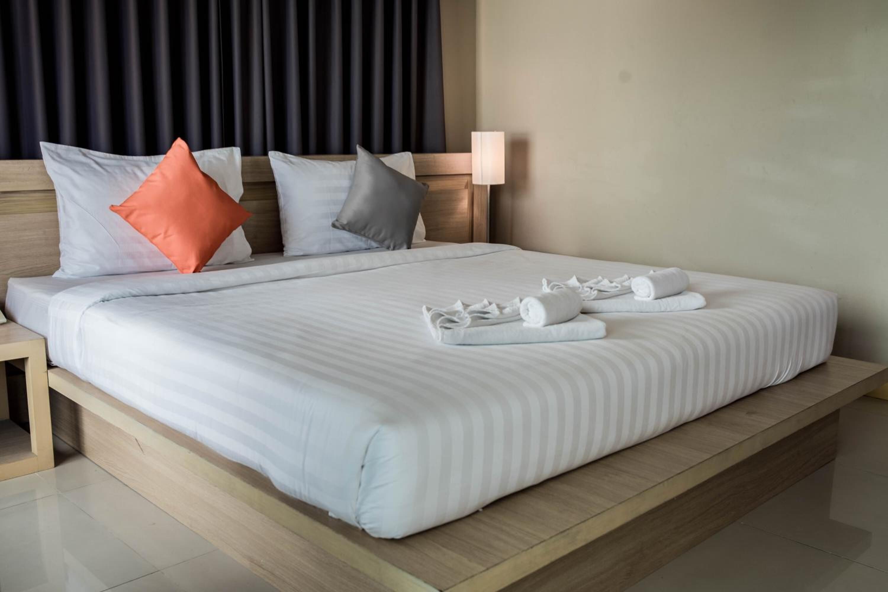 Uma cama bem arrumada com roupa de cama branca, uma cabeceira de madeira e uma mesa de cabeceira com abajur.