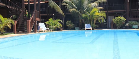 Uma piscina com espreguiçadeiras, palmeiras e um edifício com telhado de azulejos.