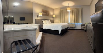 Quarto de hotel com cama grande, banheiro separado com banheira, escrivaninha e uma cadeira.