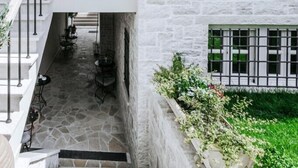 Um edifício de pedra de vários andares com uma placa que diz "ITS KALE BOUTIQUE HOTEL". Há áreas de estar ao ar livre com mesas e cadeiras, e uma pequena varanda com um vaso de flores.