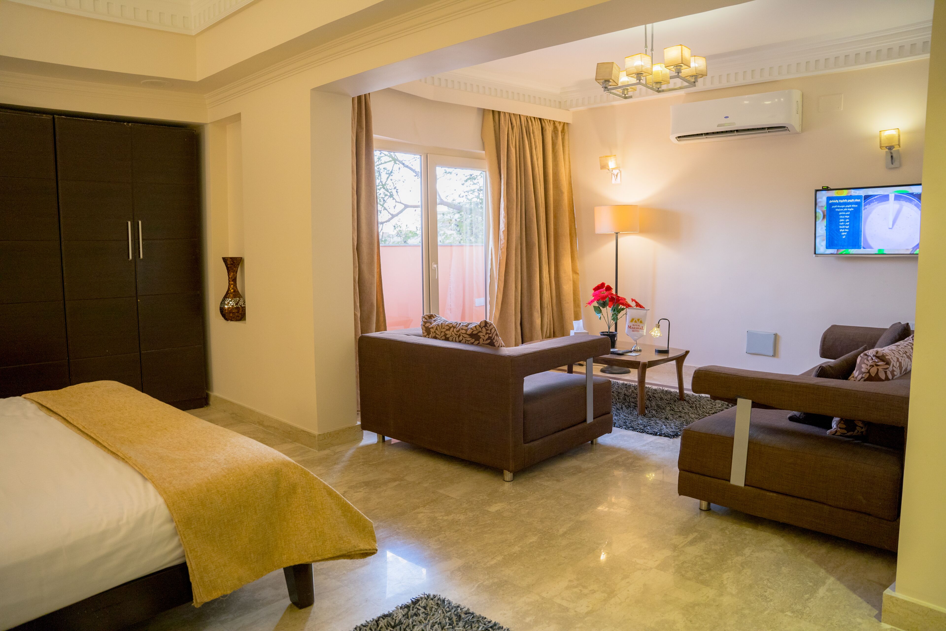 Quarto de hotel com uma cama, dois sofás, uma mesinha com abajur e uma TV na parede.