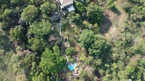 Vista aérea de uma propriedade com um edifício principal, uma construção secundária e uma piscina rodeada por vegetação densa.