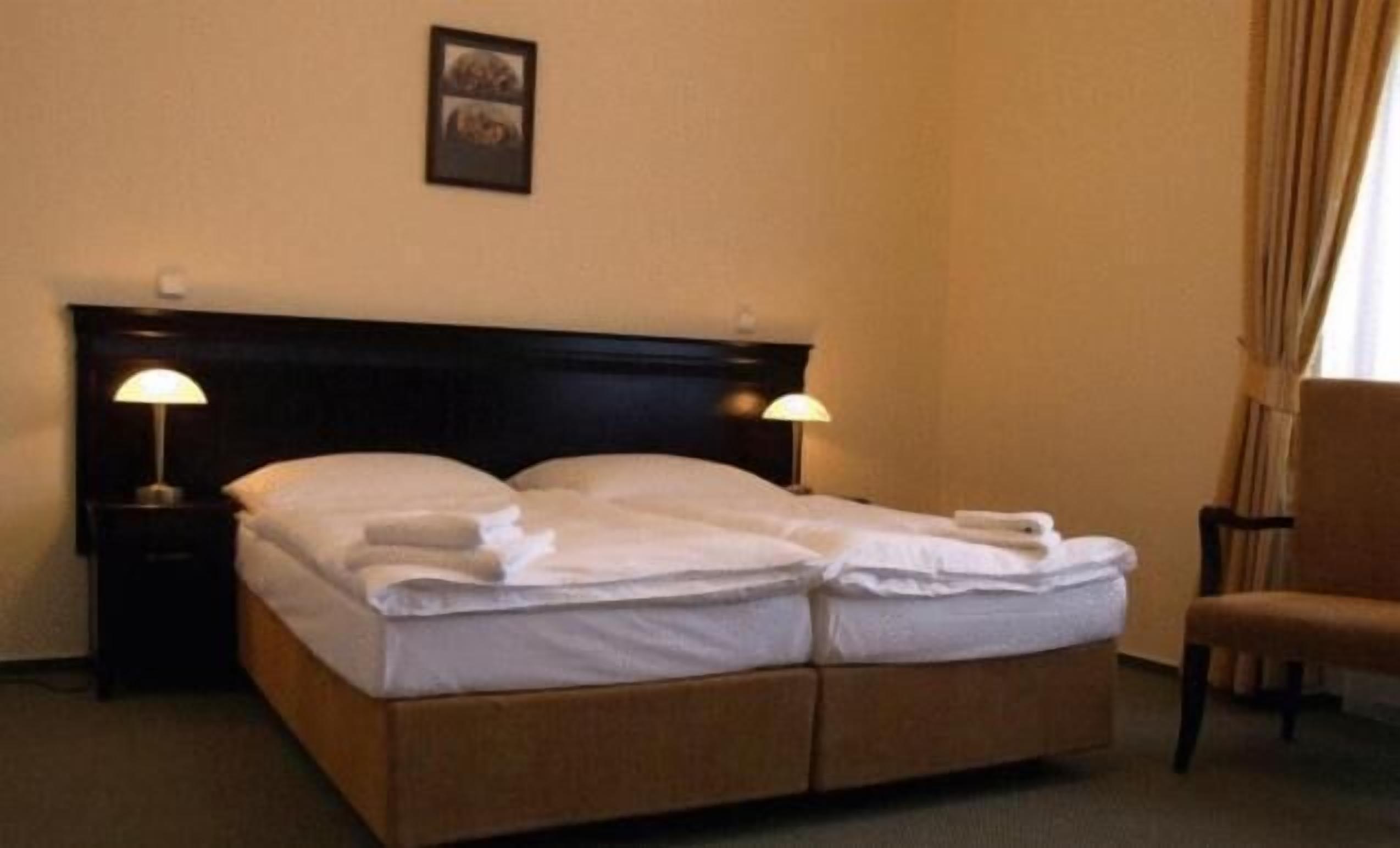 Quarto de hotel com cama de casal, duas luminárias de cabeceira, uma cadeira e um quadro na parede.