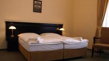 Quarto de hotel com cama de casal, duas luminárias de cabeceira, uma cadeira e um quadro na parede.