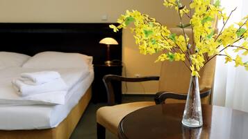 Quarto de hotel com uma cama bem arrumada, um vaso com flores amarelas sobre uma mesa e uma cadeira.