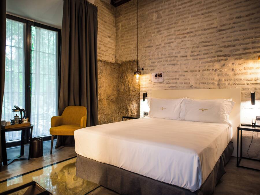 Quarto de hotel com uma cama grande, uma cadeira, uma mesa com abajur e uma parede de tijolos.