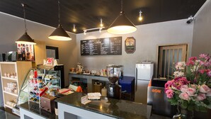 Um café com um quadro de cardápio, uma máquina de café e um vaso de flores.
