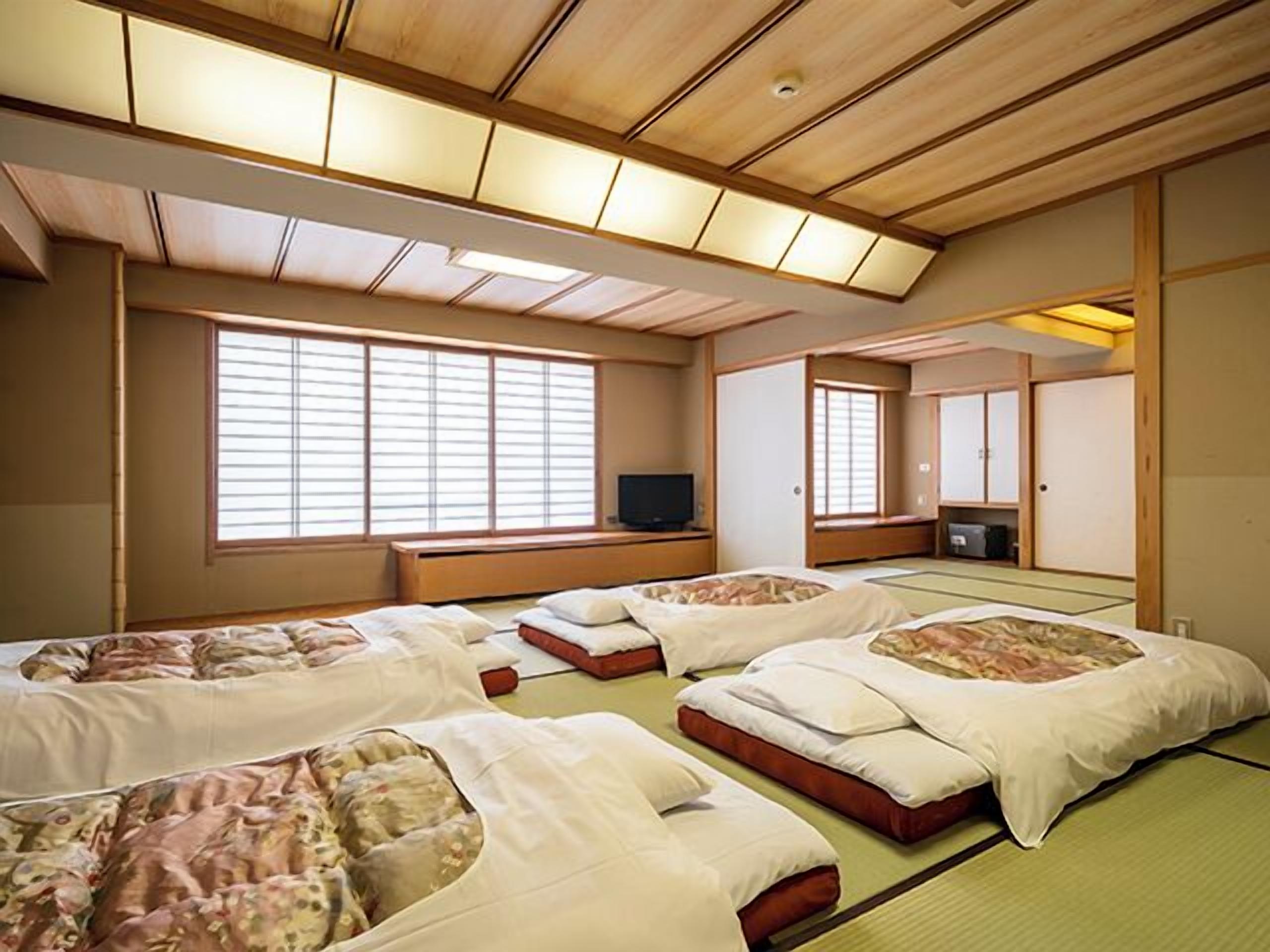 Quarto em estilo japonês tradicional, com tatames, várias colchonetes, portas corrediças e uma televisão.