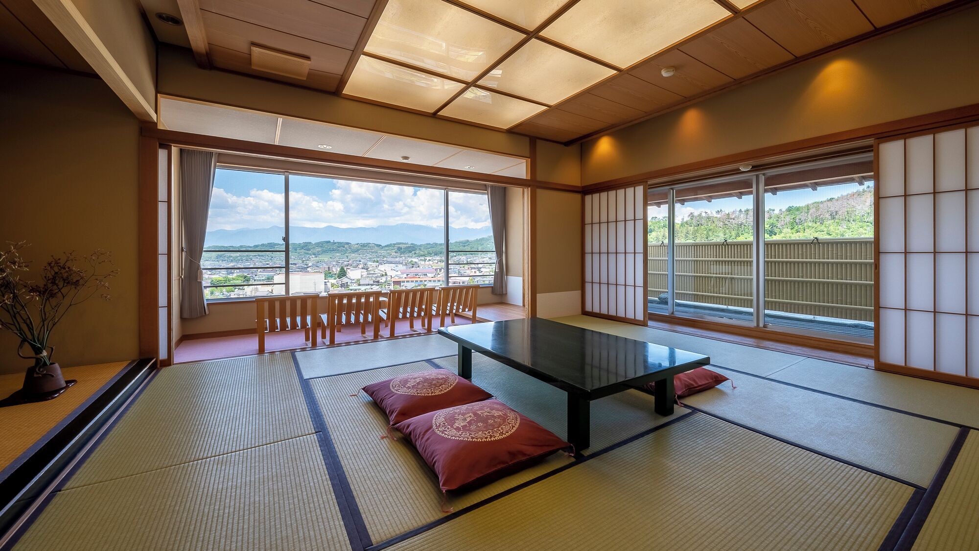 Um espaço com tatames, uma mesa baixa e almofadas, janelas amplas com vista para um horizonte urbano e montanhas, e portas corrediças.