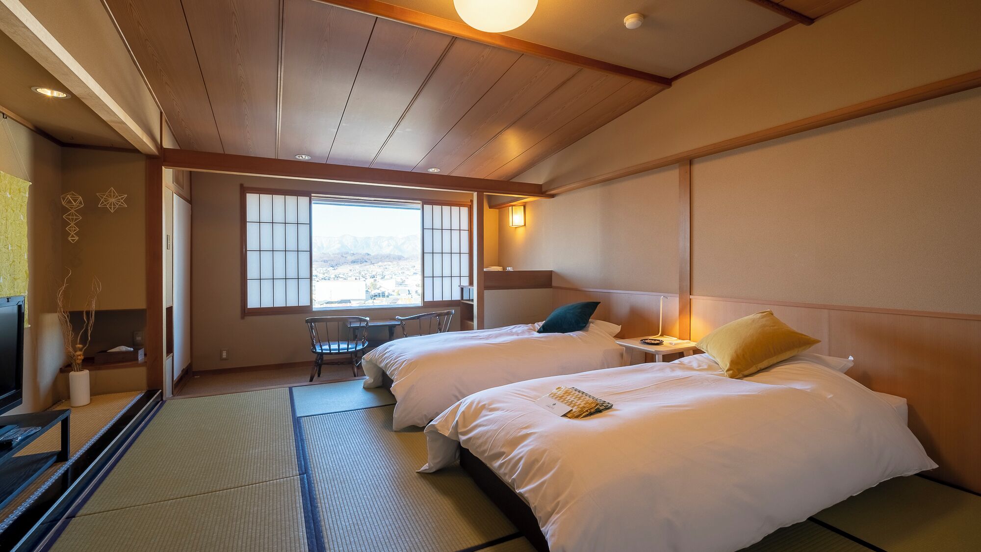 Quarto de hotel com duas camas, uma escrivaninha, uma cadeira e uma janela grande com vista.