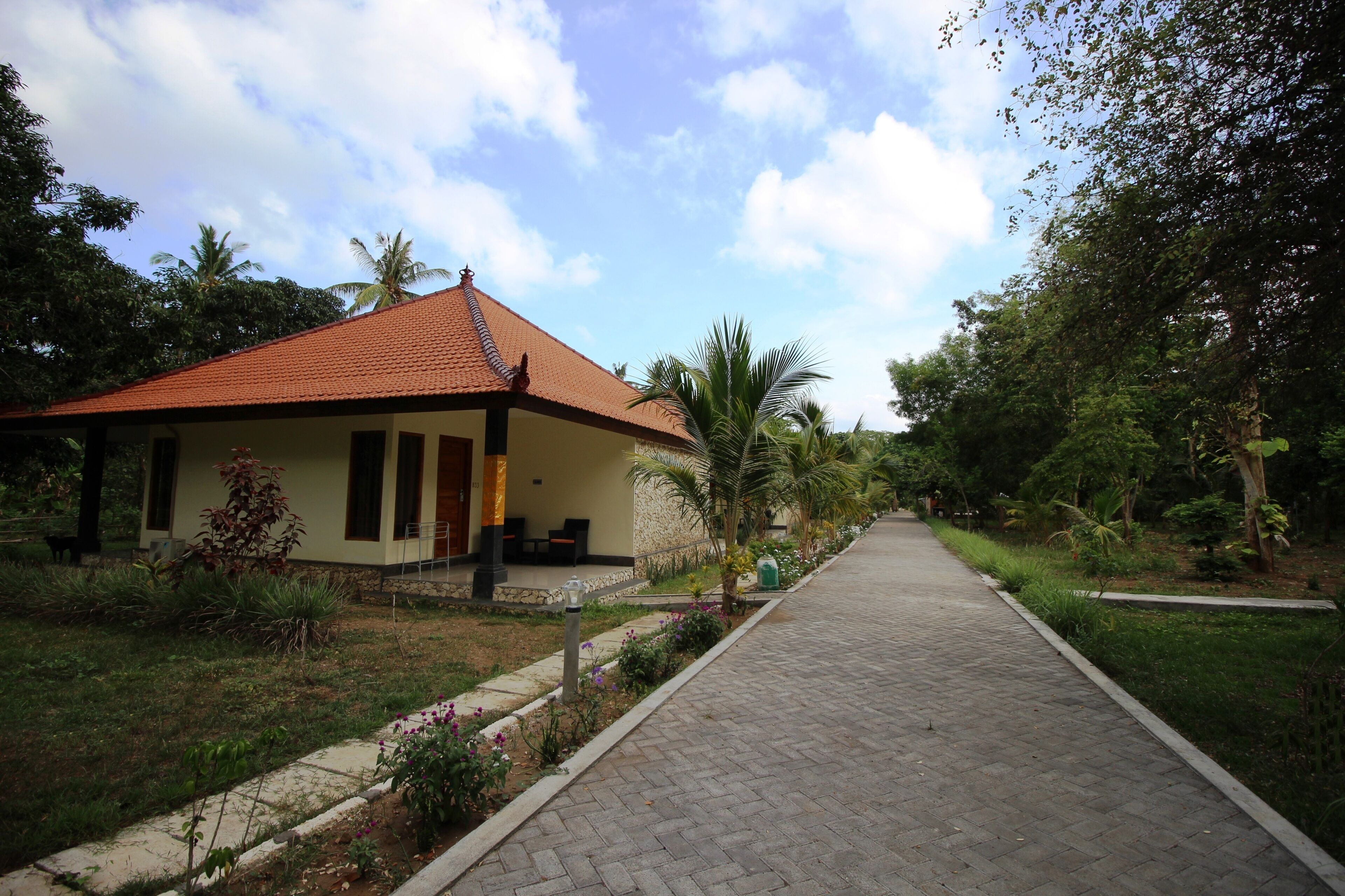 Uma casa com telhado de cerâmica, um caminho pavimentado e vegetação ao redor.