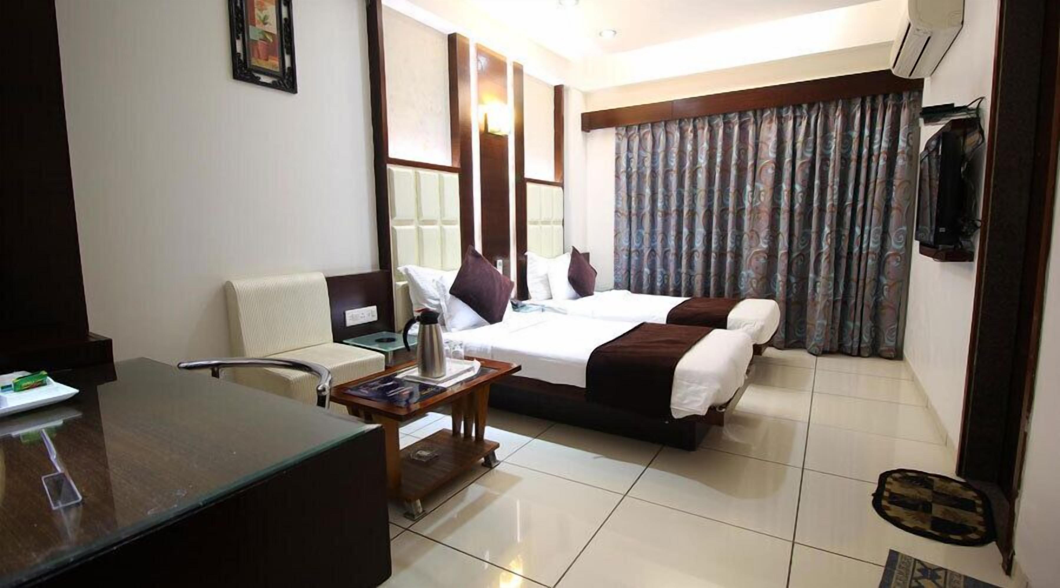 Quarto de hotel com cama, escrivaninha, cadeira e janela com cortinas.