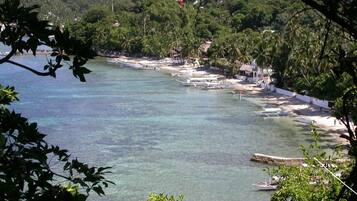 Vista costeira com água cristalina, barcos e uma área de praia com edifícios e árvores.