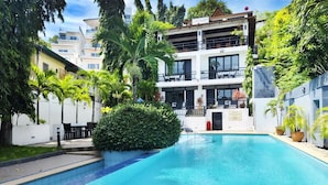 Uma piscina rodeada por vegetação exuberante e um edifício com várias janelas e varandas.