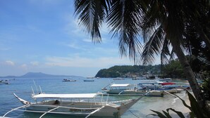 Uma praia com barcos atracados perto da costa, palmeiras e uma montanha ao longe.