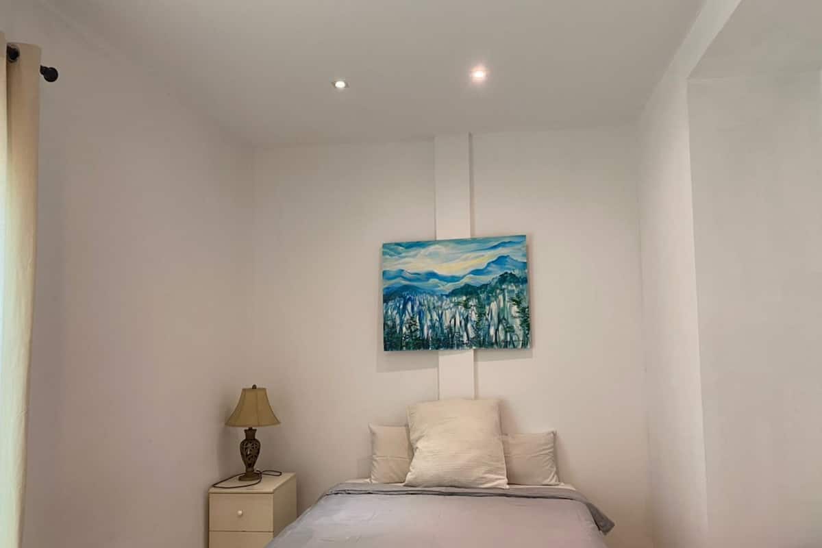 Quarto com uma cama, mesa de cabeceira, abajur e um quadro na parede.