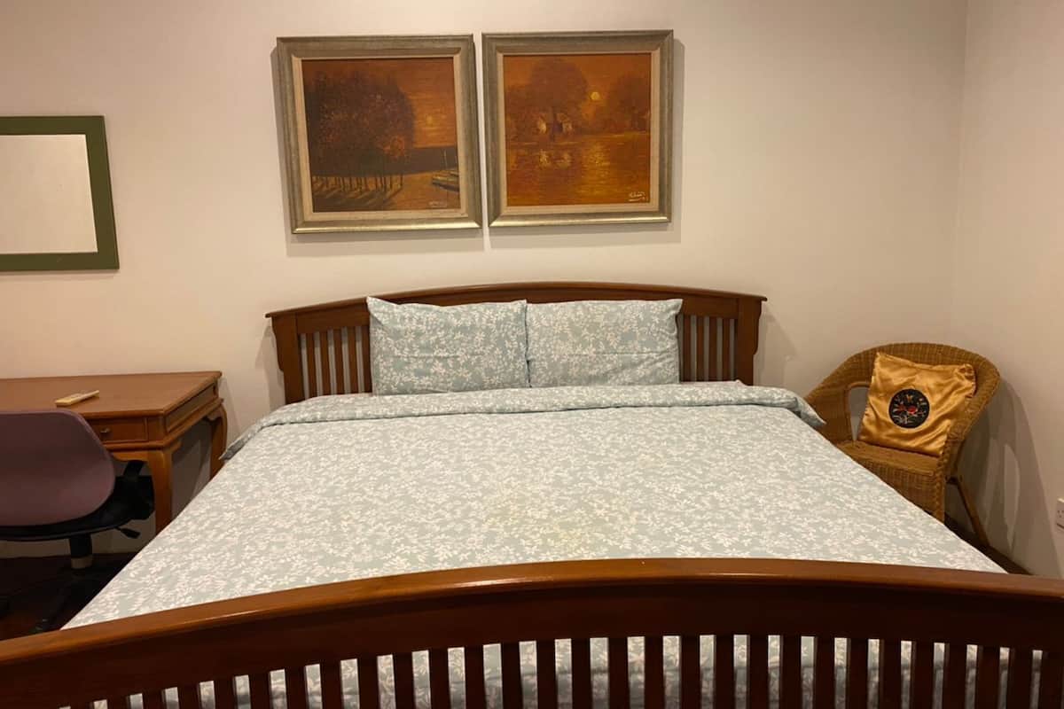 Quarto com cama de madeira, uma escrivaninha, uma cadeira e duas pinturas emolduradas na parede.