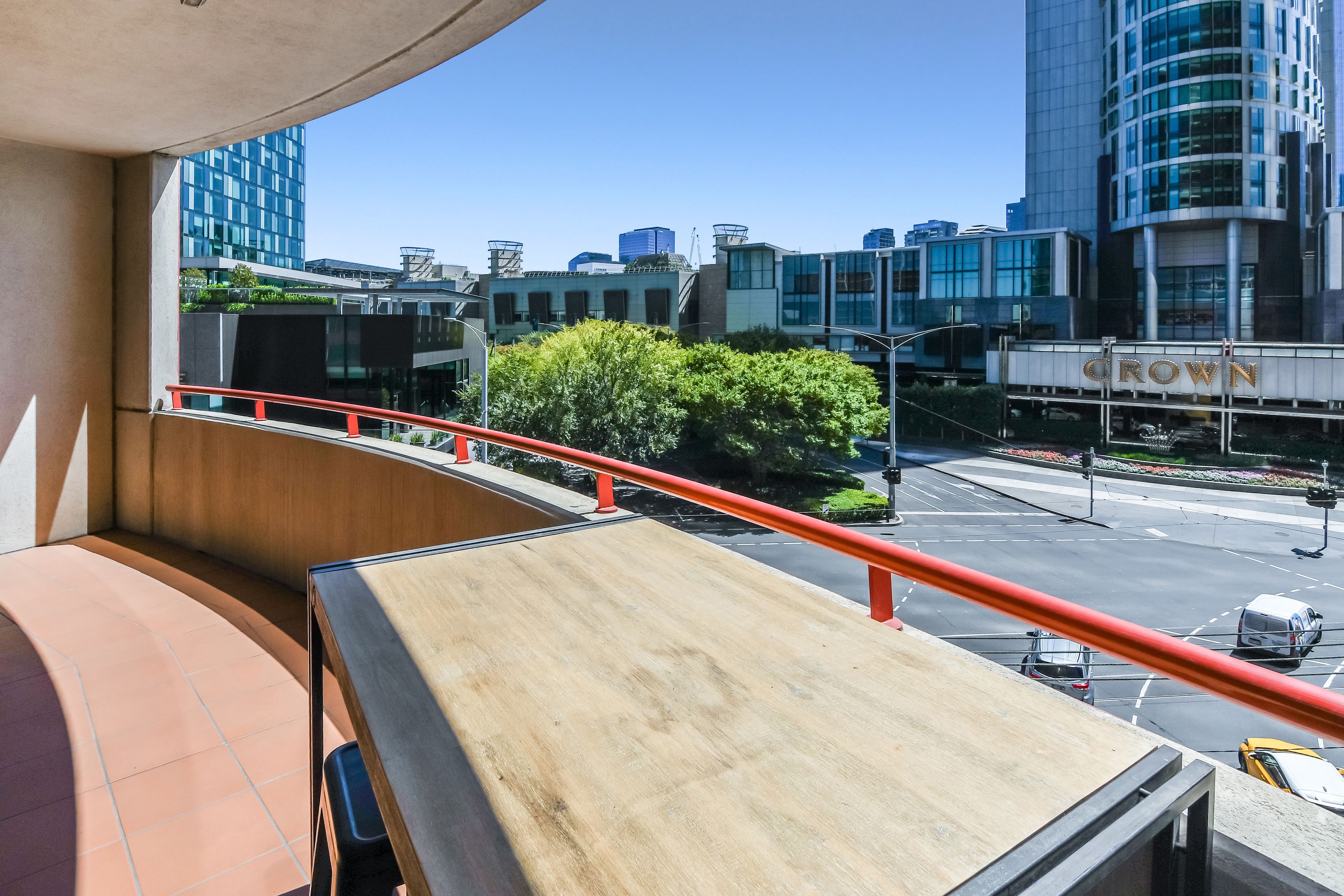 Um edifício moderno com varanda curva, guarda-corpo vermelho e vista para o horizonte urbano, incluindo um edifício com a inscrição 