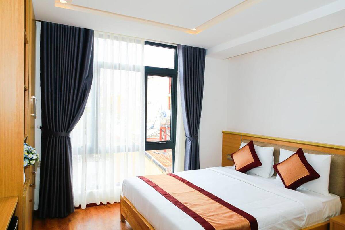 Quarto de hotel com uma cama grande, cabeceira de madeira e vista para uma varanda através de cortinas leves.