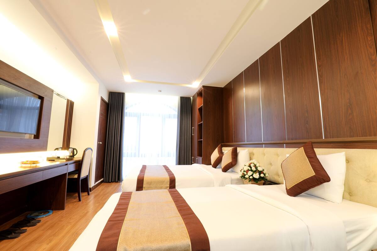 Quarto de hotel com duas camas, uma escrivaninha e um espelho grande.