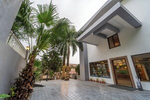 Um edifício moderno com um pátio ladrilhado, palmeiras e uma pequena janela.