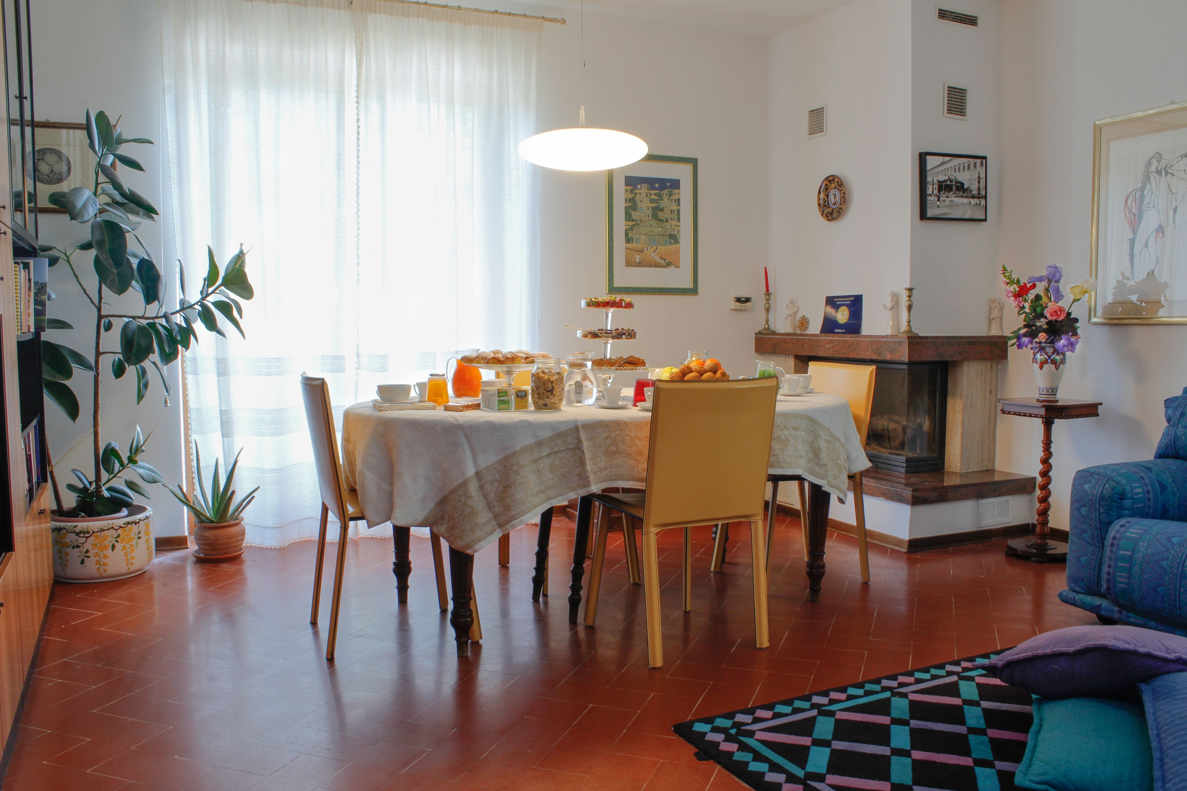 Uma sala de estar com área de refeições, mesa posta para quatro pessoas, lareira e sofá.