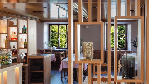 Restaurante com móveis de madeira, copos de vidro e vista para o verde lá fora.