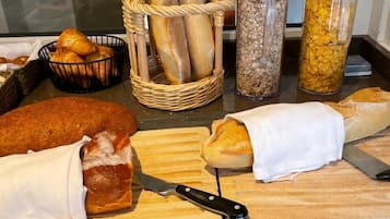 Uma bancada de cozinha com vários pães, um cesto de croissants, um pote de aveia e um pote de sementes de girassol.
