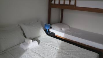 Uma cama beliche com roupa de cama branca, um abajur azul e uma pequena mesa com um controle remoto.