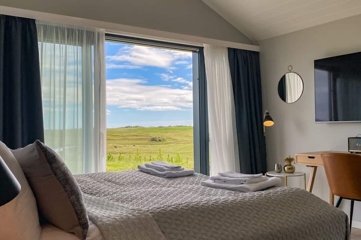 Quarto com uma cama grande, uma escrivaninha, uma cadeira, uma TV e vista para uma paisagem verde.