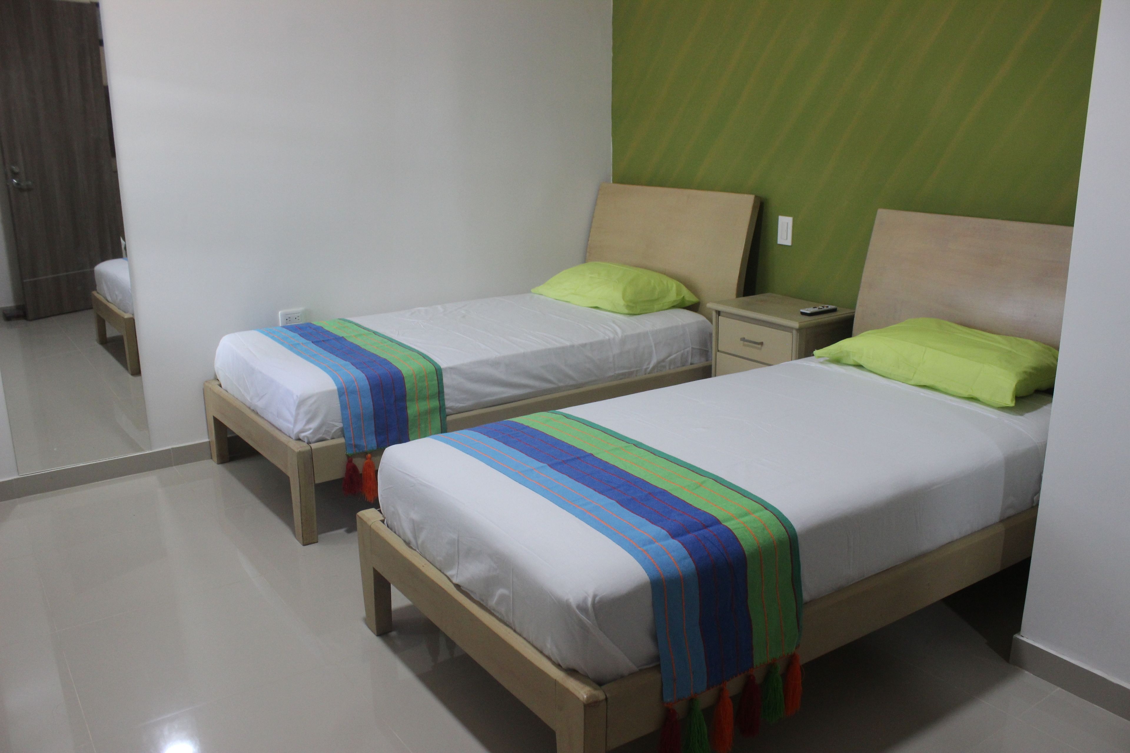 Duas camas de solteiro com estrutura de madeira e roupa de cama branca, cada uma com um cobertor listrado e colorido.