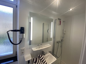 Uma casa de banho moderna com um espelho grande, um chuveiro, uma pia e um secador de cabelo fixado na parede.